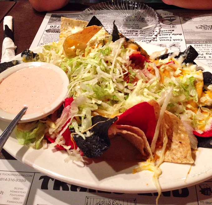 Buffalo chicken nachos piled high enough to require structural engineering knowledge and an ambitious appetite.