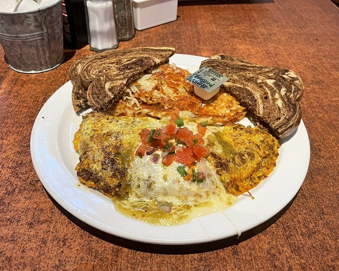 An omelet that's having an identity crisis as a work of art, with marble rye toast standing by for support and hash browns for moral guidance.