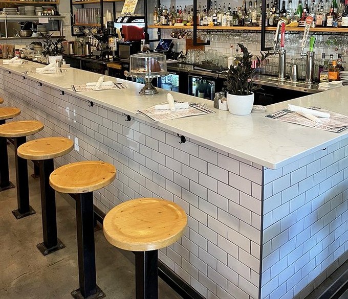 Clean white subway tile meets warm wooden counter seating. The perfect perch to watch culinary magic happen while nursing your morning coffee.