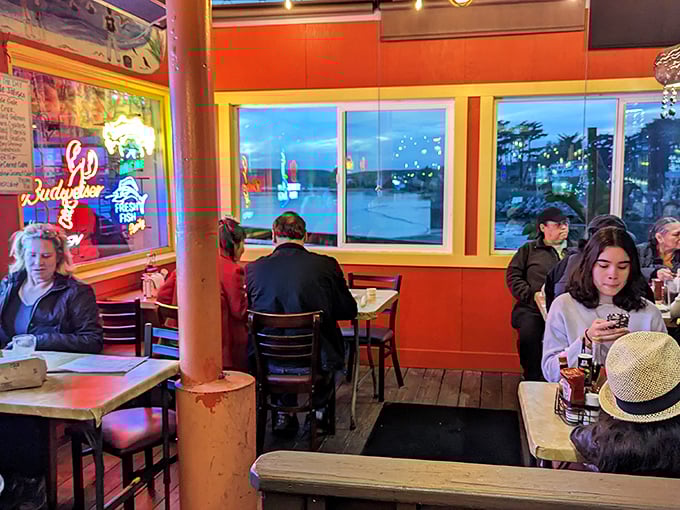 Evening diners bask in the warm glow of neon signs and harbor lights. Some conversations just taste better with seafood and sunset views.