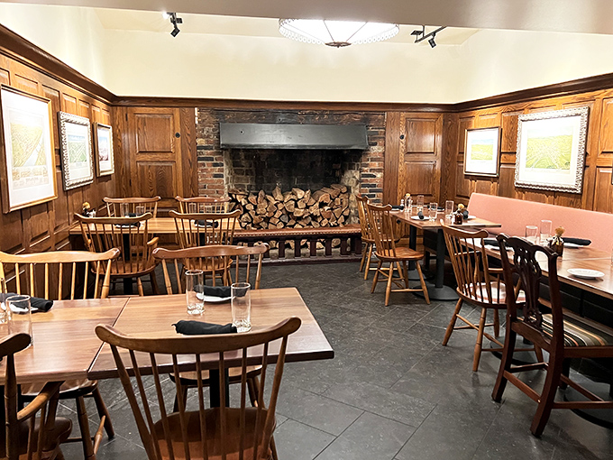 A fireplace loaded with wood stands ready in this dining room where Windsor chairs and warm paneling create the perfect gathering space.