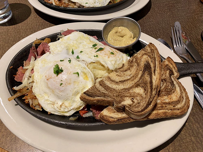 Marbled rye toast stands at attention beside a skillet where eggs, potatoes and savory delights mingle in perfect breakfast harmony.