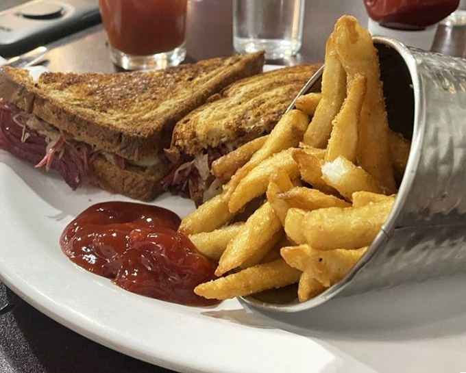 The Reuben sandwich, where pastrami and sauerkraut perform a perfect culinary tango, while golden fries wait patiently in their metal sidecar for their moment.