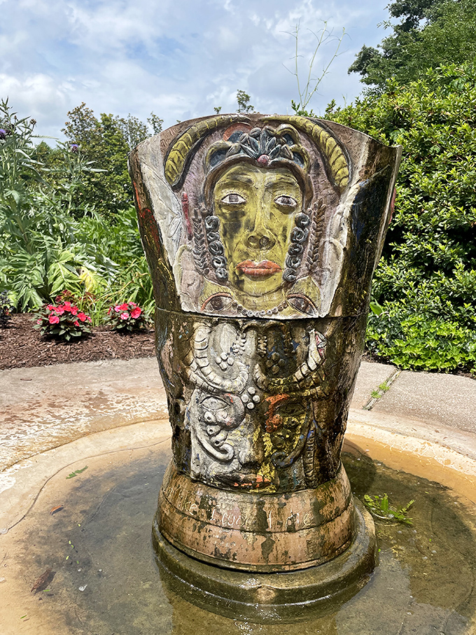 An ornate sculptural fountain stands as garden centerpiece, its weathered face suggesting it's seen generations of visitors come and go.