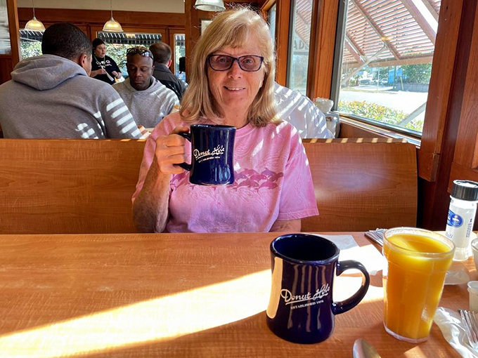 A satisfied customer raises her Donut Hole mug like a trophy. That orange juice looks like liquid sunshine in a glass.