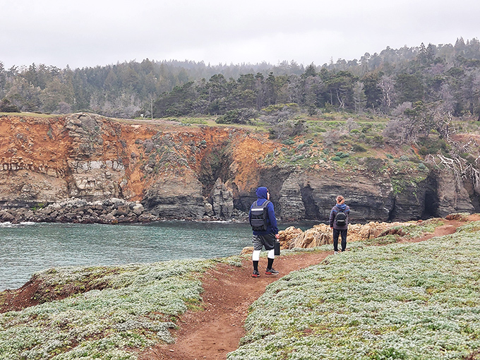Two hikers follow the trail of countless explorers before them. The red soil path contrasts dramatically with the coastal palette.