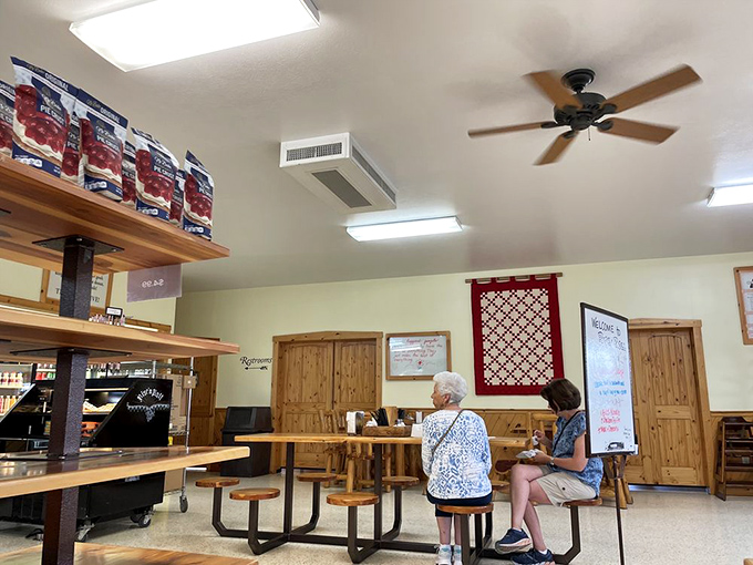 Simple seating, wooden accents, and red quilted wall hangings create an atmosphere where conversations flow as freely as the coffee.