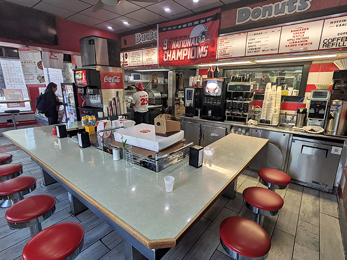 The counter where magic happens—stainless steel, red stools, and enough Ohio State memorabilia to make a Michigan fan twitch nervously.