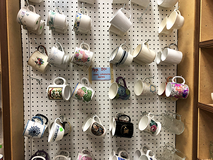 A pegboard of personality where coffee mugs hang like colorful ornaments, each one advertising someone's abandoned hobby, vacation, or workplace.