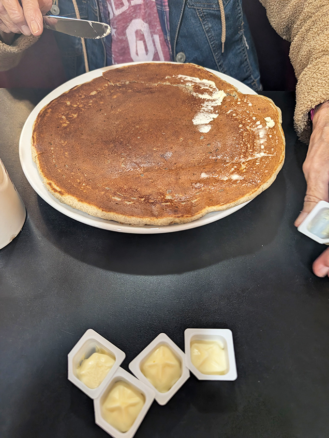 A pancake so perfectly round and golden it could make the moon jealous. Four butter pats standing by for their delicious sacrifice.