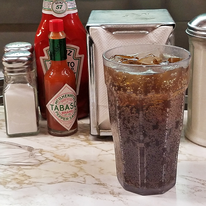 The soda glass sweating beside classic condiments&mdash;a tableau of American diner perfection that Norman Rockwell would've painted.