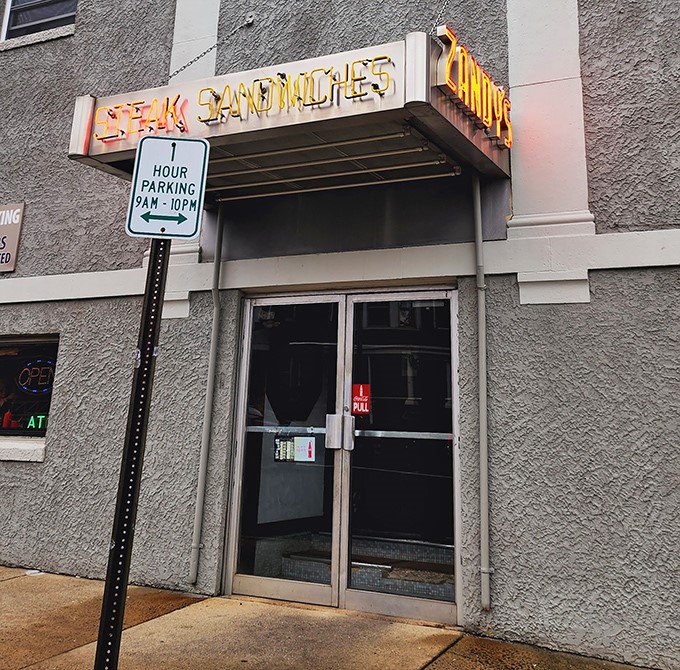 The neon "STEAK SANDWICHES" sign beckons hungry travelers like a lighthouse guiding ships to safe harbor. Follow the glow to satisfaction.