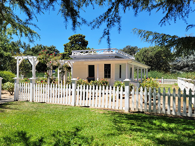 A quaint white cottage with a picket fence sits among blooming gardens offering a picture-perfect scene of simple timeless beauty.