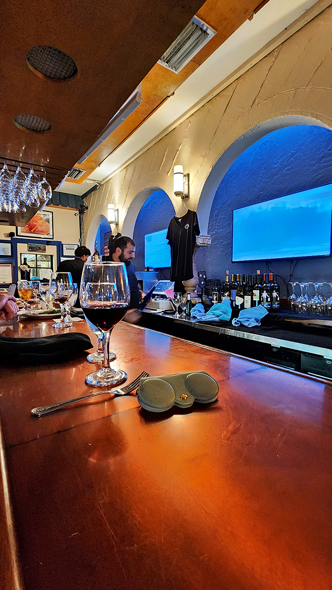 A glass of red wine awaits at the polished bar while blue-lit arches create the perfect backdrop for contemplating your next seafood selection.