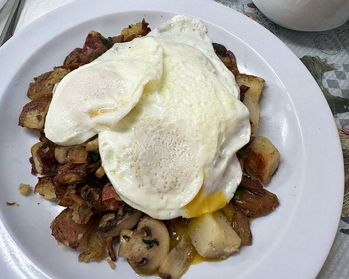 Perfectly cooked eggs atop a mountain of home fries &ndash; proof that sometimes the best breakfast architecture is a beautiful mess.