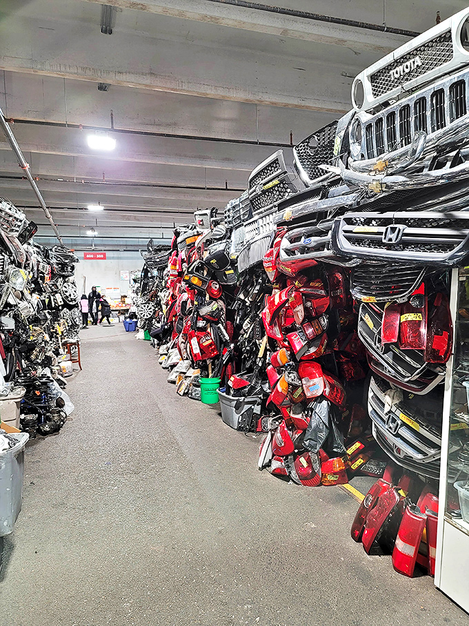 Automotive grilles stacked like metallic smiles. Car enthusiasts browse this wall of mechanical faces with the focus of art collectors.