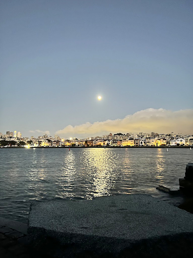 As night falls, the city lights create a glittering backdrop for the Wave Organ's evening performance&mdash;nature's nocturne with urban accompaniment.