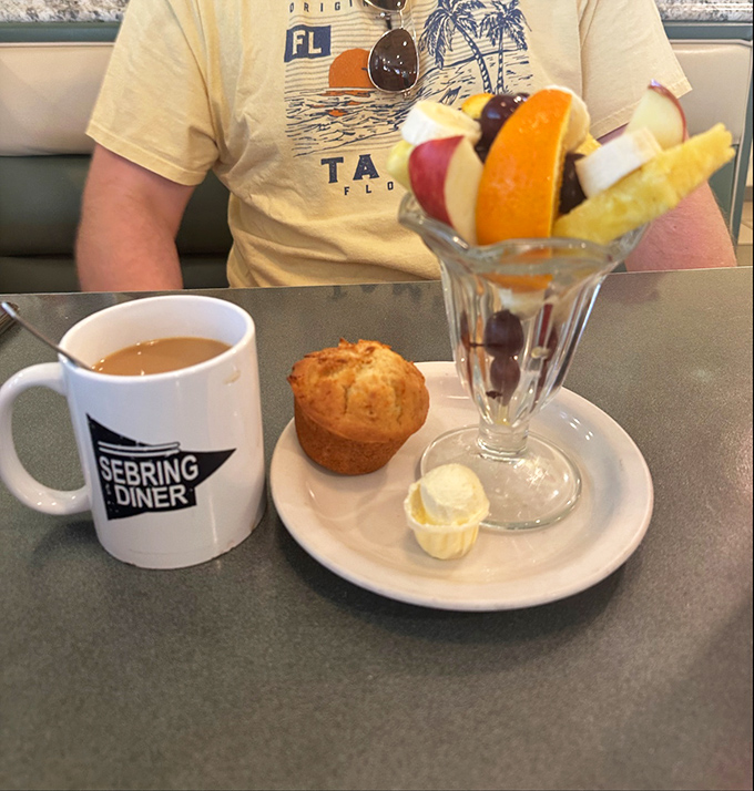 Morning salvation arrives in a branded mug, alongside a muffin and fruit cup that says "yes, you can pretend this breakfast is healthy."