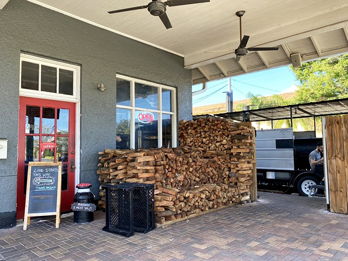 The stacked oak firewood isn't just fuel&mdash;it's the foundation of flavor, a visual reminder that great barbecue begins with proper combustion.