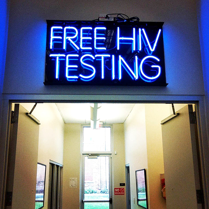 The neon "FREE HIV TESTING" sign highlights the store's mission beyond retail&mdash;providing essential health services that directly benefit from your shopping dollars. 