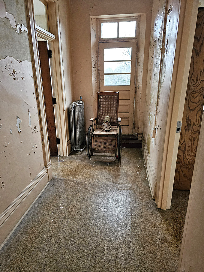 A narrow hallway leads to unknown destinations, with peeling paint recording the passage of time. The wheelchair's presence adds an eerie touch.