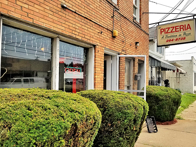 This unassuming pizzeria, with its neatly trimmed hedges, promises the kind of authentic pies that make chain restaurants weep with inadequacy.