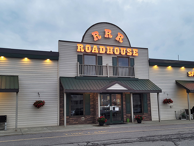 Red River Roadhouse glows with warm promise at dusk, its illuminated sign a beacon for hungry travelers seeking comfort food and conversation.