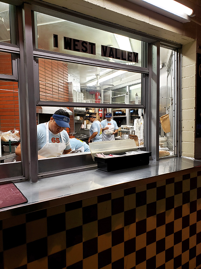 The kitchen window offers a glimpse into the organized chaos where pastrami dreams are assembled with practiced precision.