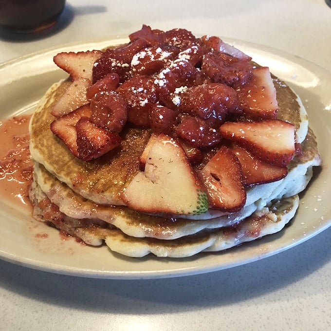 Strawberry pancakes stacked higher than your weekend expectations, crowned with berries and powdered sugar that make breakfast feel like dessert.