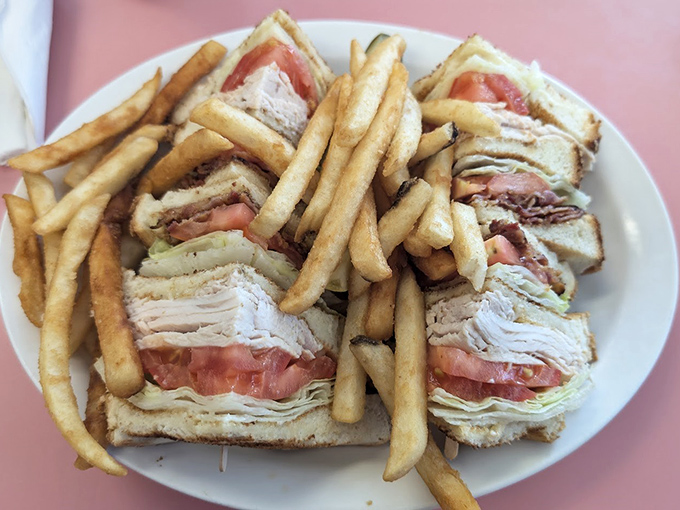 A club sandwich stacked so high it needs architectural support, with fries standing by for the inevitable moment when sandwich contents escape.