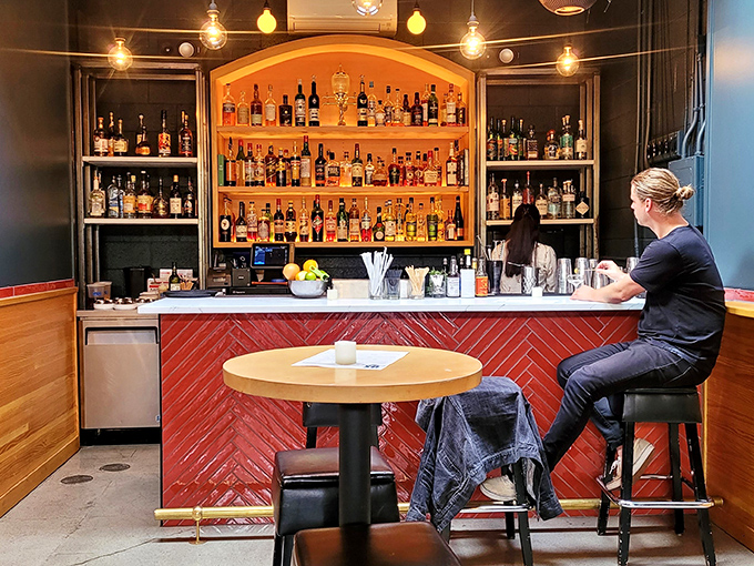 The bar's warm glow creates a halo effect around bottles that stand like soldiers, ready to enhance your meal with liquid reinforcements.