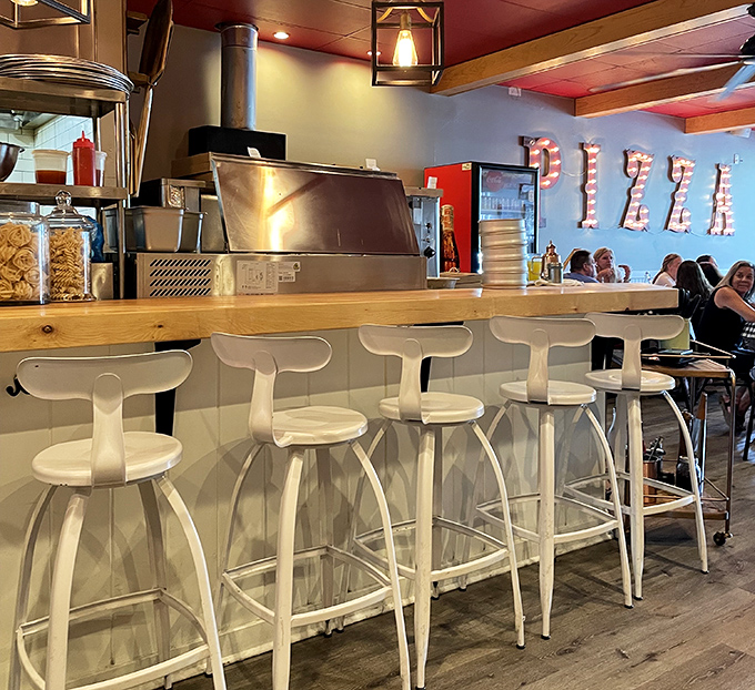 White counter stools await their next hungry patrons. Behind them, the kitchen symphony is about to begin its delicious performance.