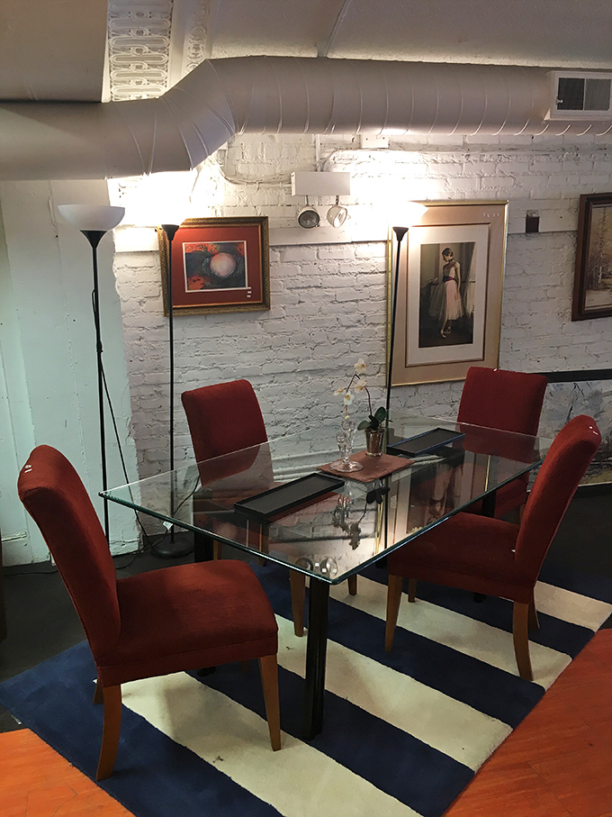 A glass dining table surrounded by red velvet chairs against exposed brick. Don Draper would approve of this mid-century moment.