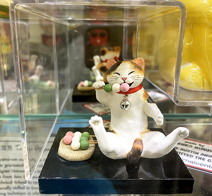 Just one more dango, please! This playful figurine captures a lucky cat enjoying traditional Japanese sweets with unmistakable feline satisfaction.