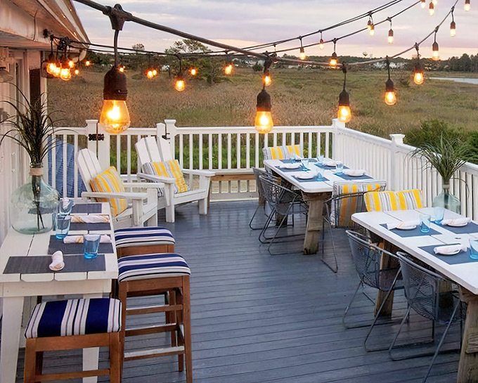 As twilight falls, string lights transform the deck into a magical dining space where salt air seasons every bite.