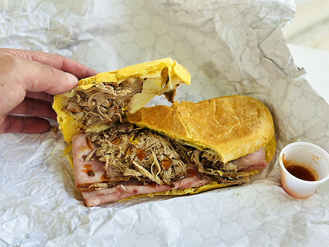 The pulled pork sandwich reveals itself like a meaty treasure chest. That glistening sauce cup on the side? Liquid gold for the initiated.