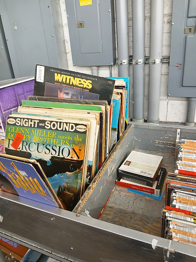 Vinyl records stand like time capsules against utility pipes, offering musical journeys from Glenn Miller to movie soundtracks of yesteryear.