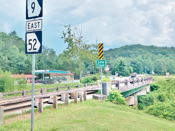 Highway signs point the way over Cane Creek Bridge, where the journey through rolling green hills becomes as memorable as the destination.