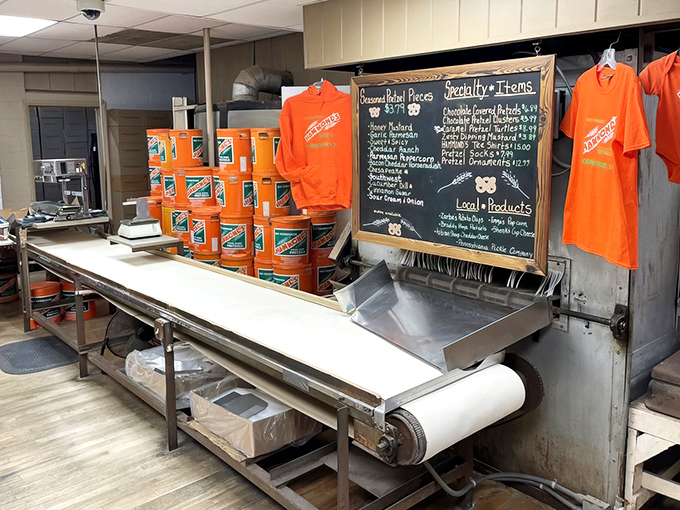 The conveyor belt of dreams, where twisted dough begins its journey to pretzel perfection. Orange t-shirts add a pop of color to this working bakery.