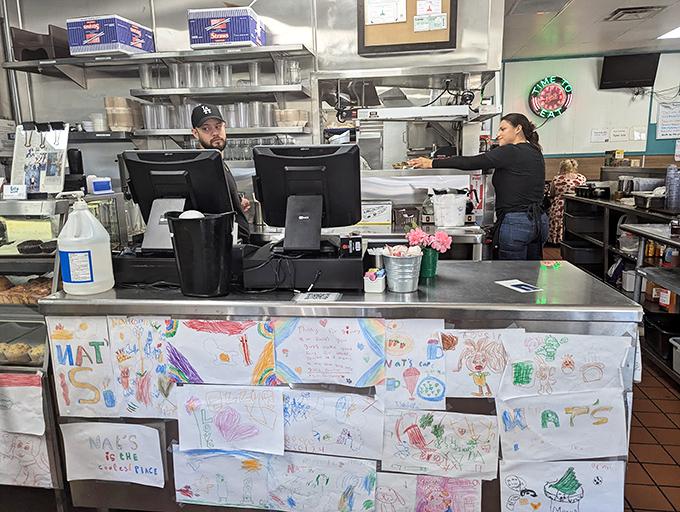The counter where regulars perch, watching breakfast choreography while children's artwork provides the most honest restaurant reviews.