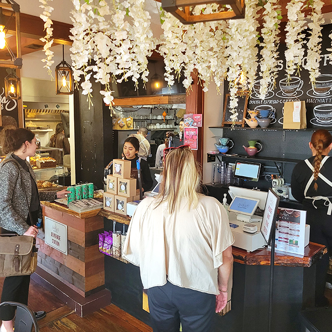 Morning rituals unfold at the ordering counter, where hanging white florals create the sensation of dining beneath a blooming spring garden, regardless of season.