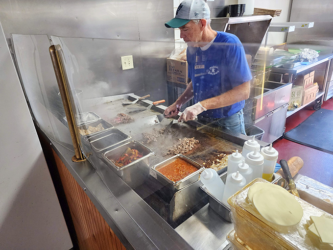 The griddle master at work, wielding metal spatulas with the precision of a surgeon and the confidence of someone who's made thousands of perfect cheesesteaks.