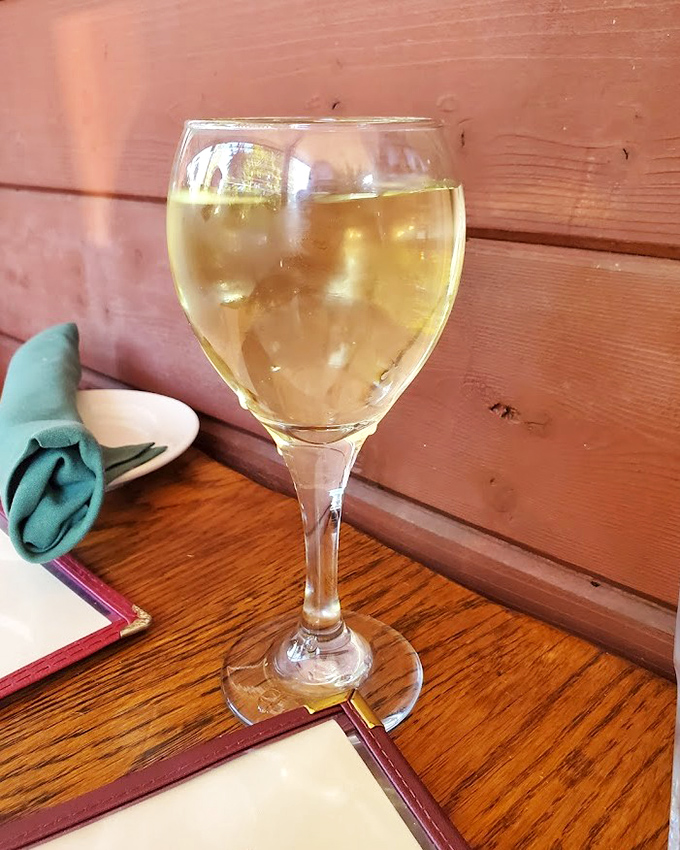 A glass of crisp white wine against rustic wood &ndash; like a little poem about the perfect marriage of refinement and comfort that defines this place.