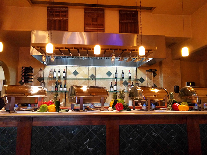 The buffet setup gleams with possibility, colorful vegetables standing guard beside silver chafing dishes of untold delights.