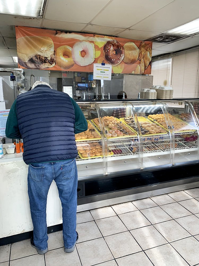 The universal morning ritual: a customer contemplating life's most important decision while the donuts patiently await their fate behind glass.