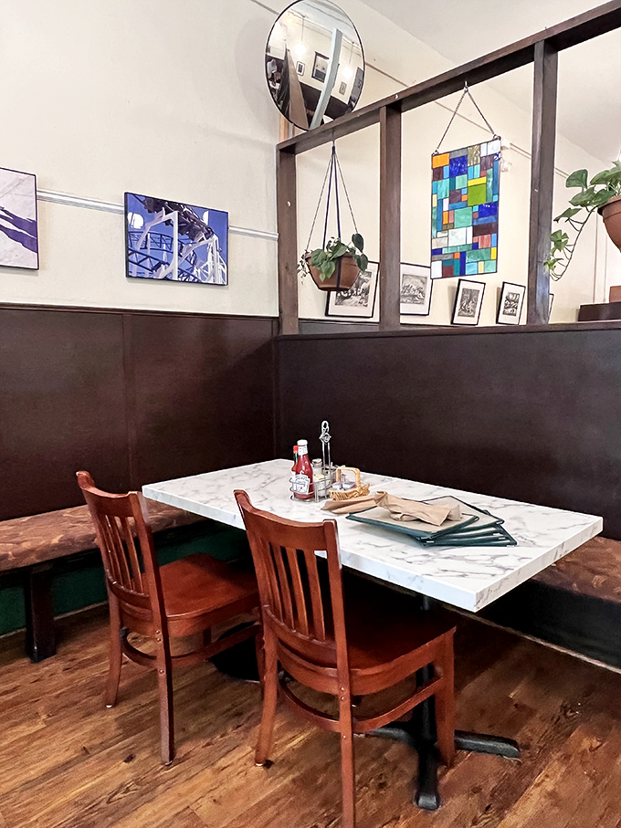 Cozy booth seating separated by stained glass dividers creates little breakfast sanctuaries. The hanging plants add a touch of life to conversations already buzzing with energy.