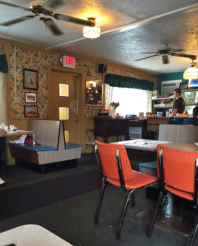 The dining room's charm lies in its unpretentious authenticity &ndash; ceiling fans, exit signs, and floral wallpaper creating a time capsule of American dining.