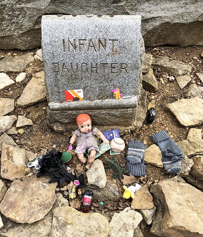 The infant daughter marker has become a shrine of offerings – dolls, mittens, and toys left by visitors moved by a tragedy from another century.