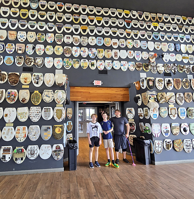 Families pose amid hundreds of decorated toilet seats. The sheer volume of the collection creates an immersive art experience.