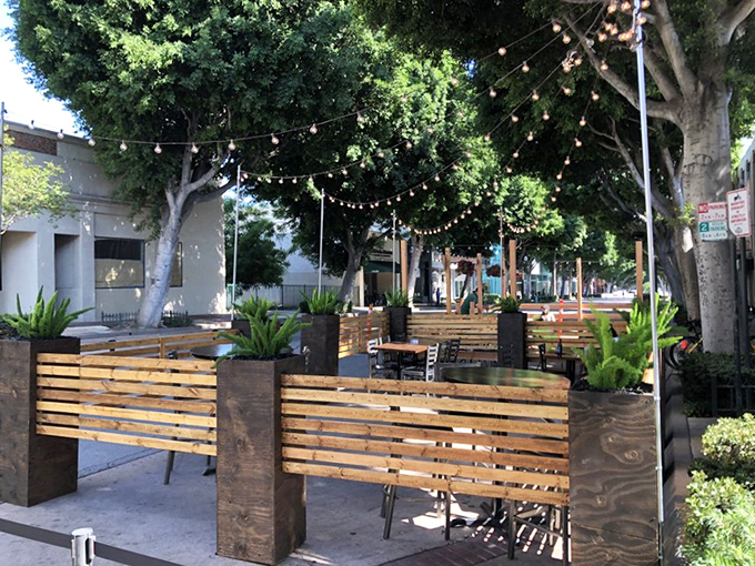 Outdoor seating under string lights and trees creates an urban oasis where summer evenings stretch deliciously into night.